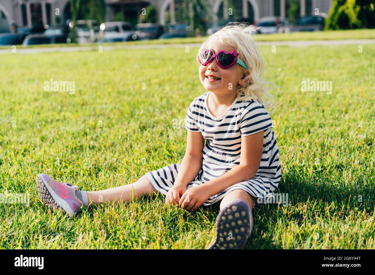 Happy smiling little girl sits on a lawn in an urban environment Stock ...