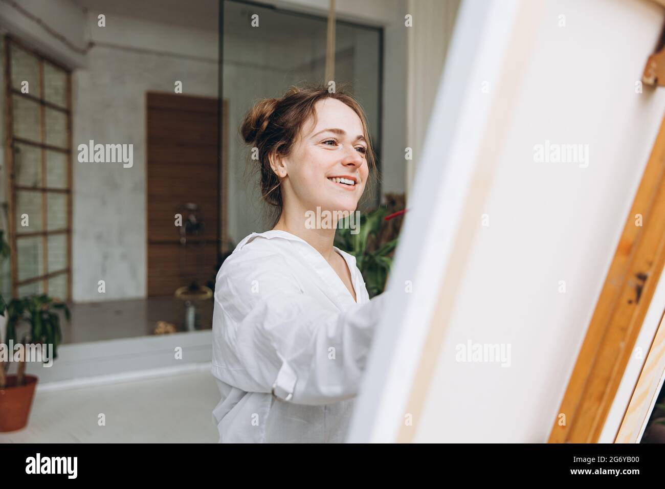 Smiling inspired artist painting with brush on easel Stock Photo - Alamy