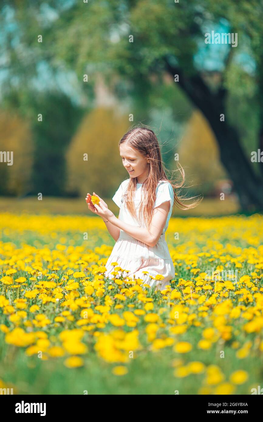 Little blonde girl pick flowers in a meadow full of yellow dandelions ...