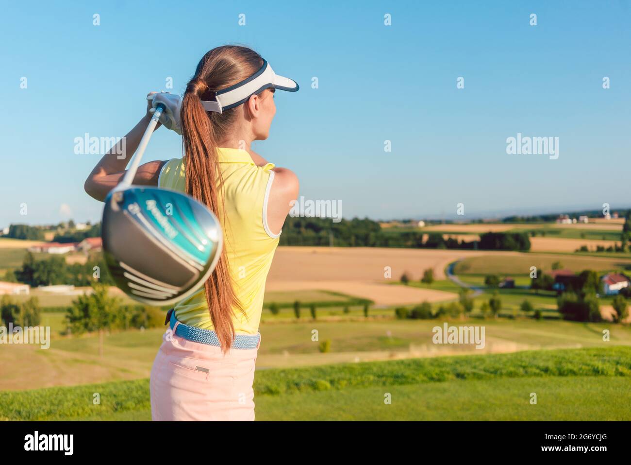 Young woman holding a driver club behind her back during golf swing, at ...