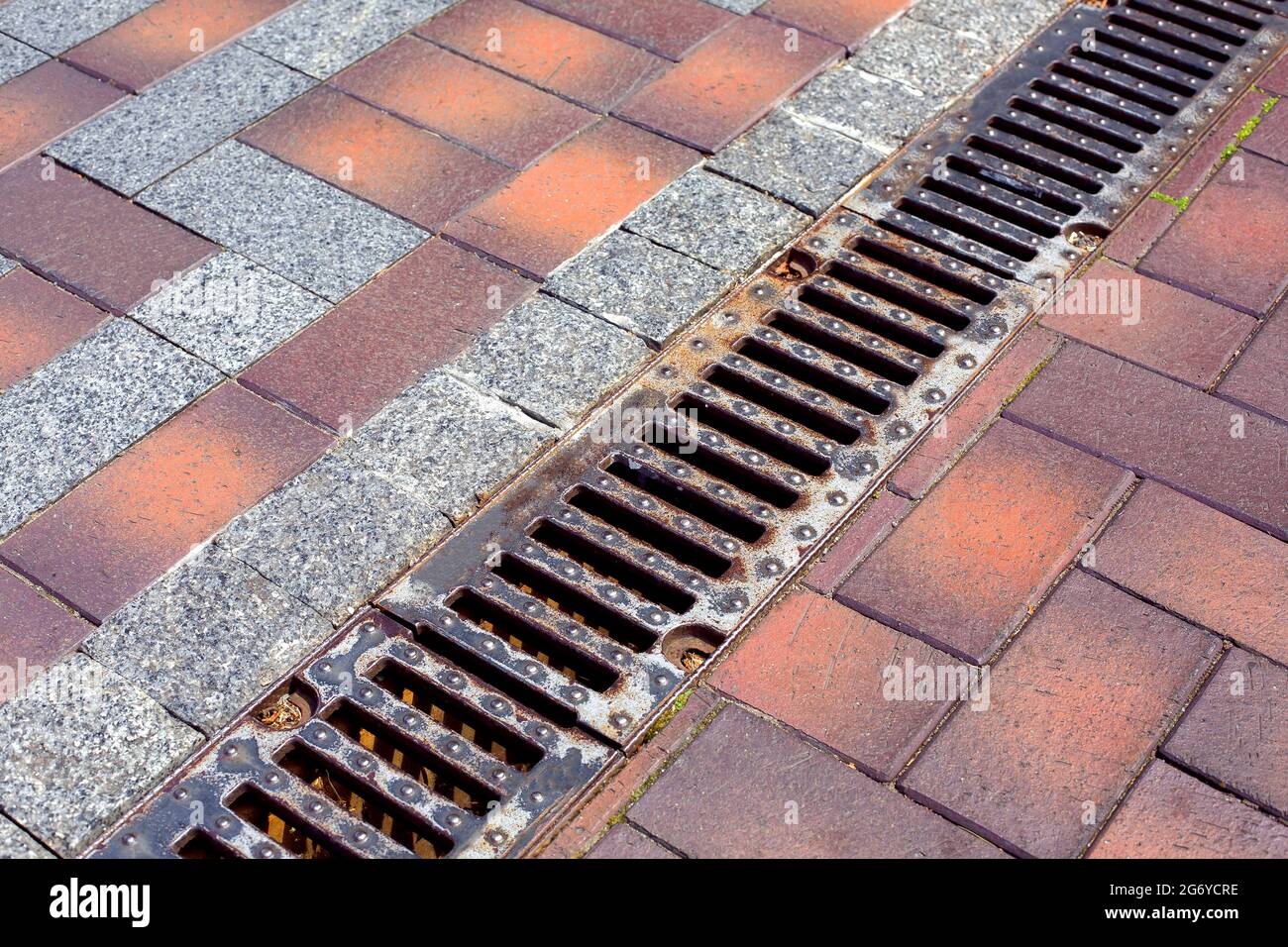 a drainage ditch covered with an iron grate on a sidewalk made of stone ...