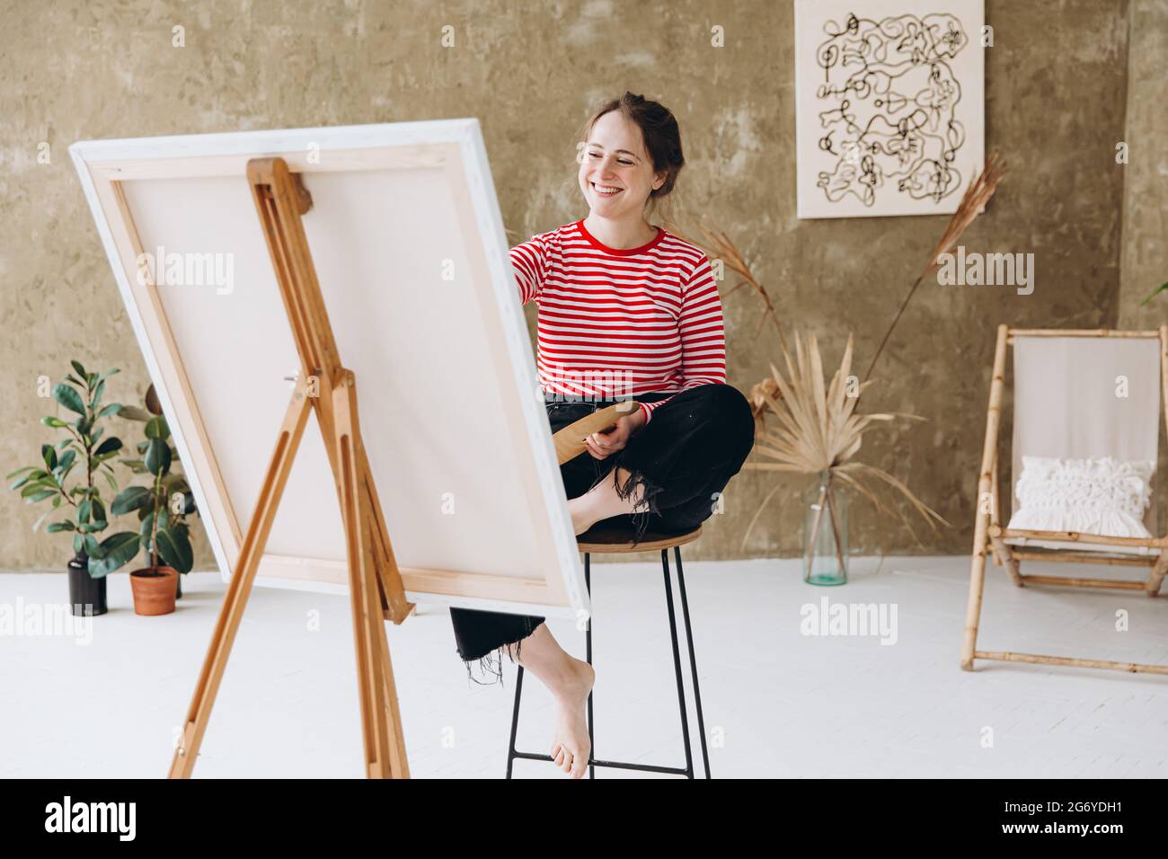 Cheerful female artist painting on easel at studio Stock Photo - Alamy