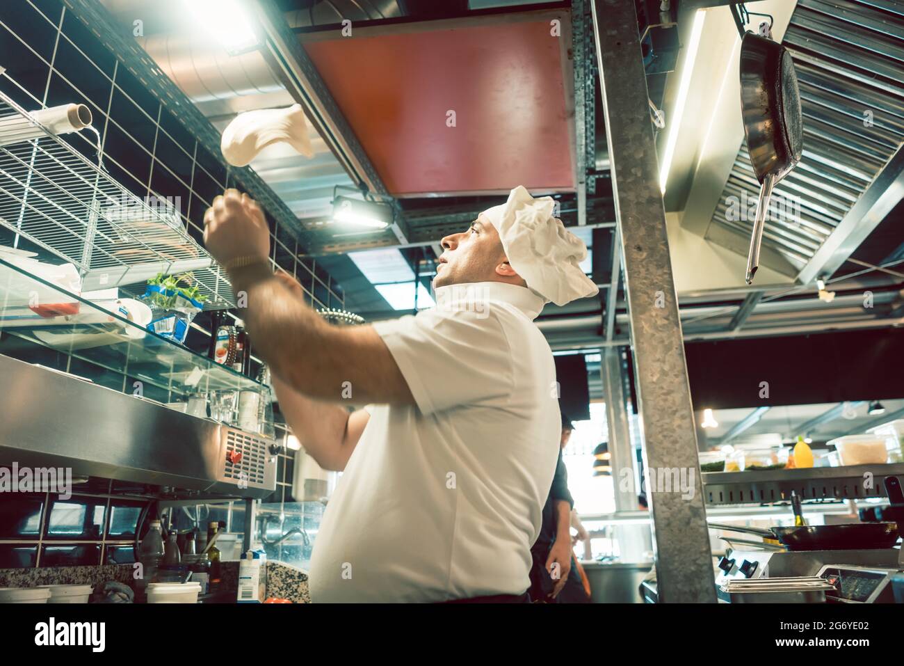 Low-angle side view of an experienced cook tossing dough while ...
