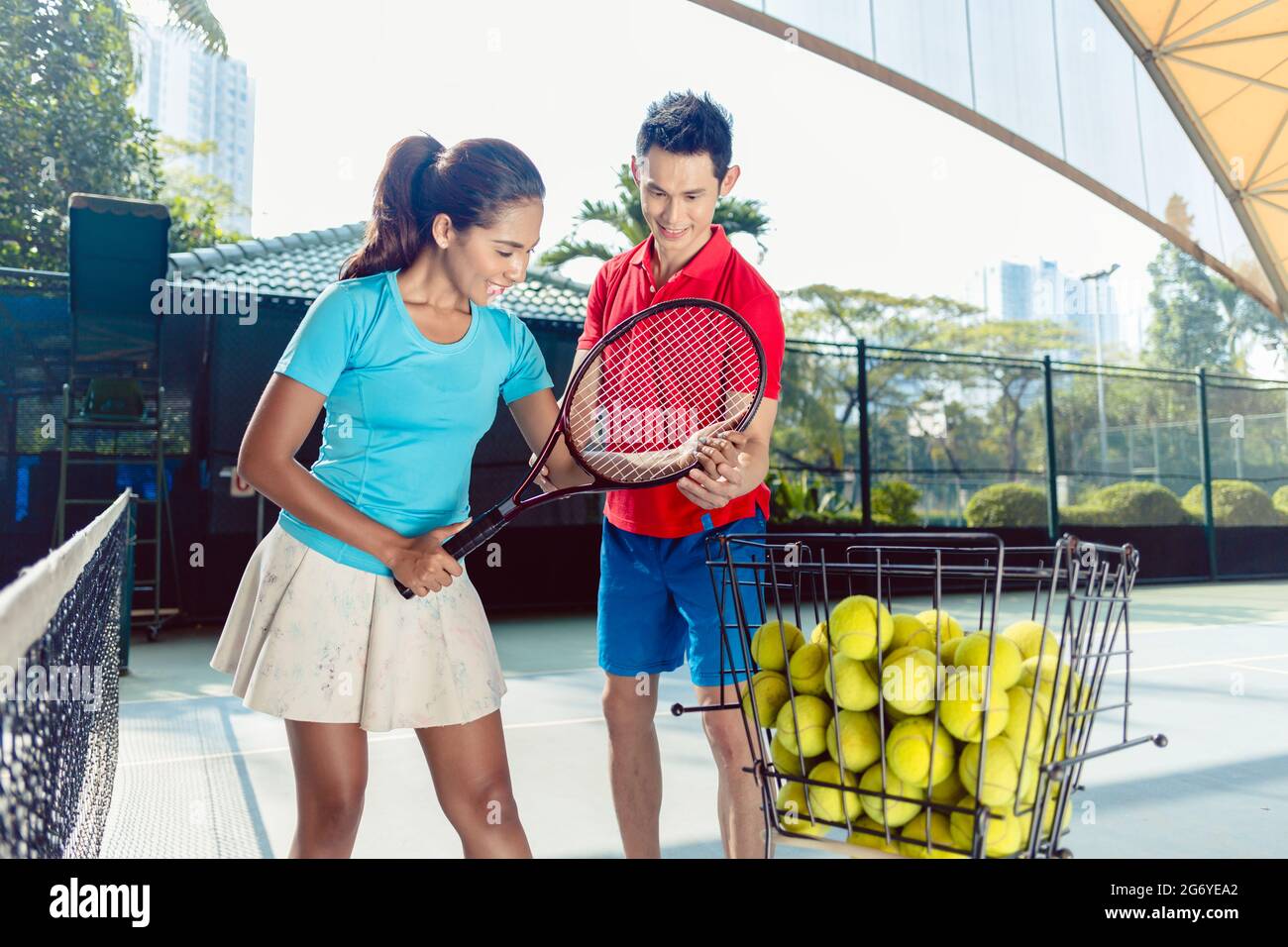 Chinese Tennis Instructor Smiling While Teaching A Beginner Female