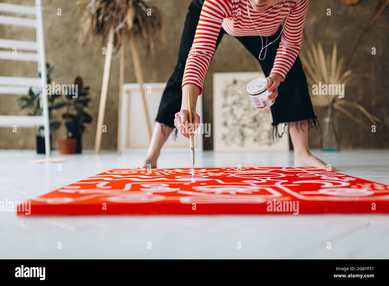 Female artist in earphones painting on red canvas Stock Photo - Alamy