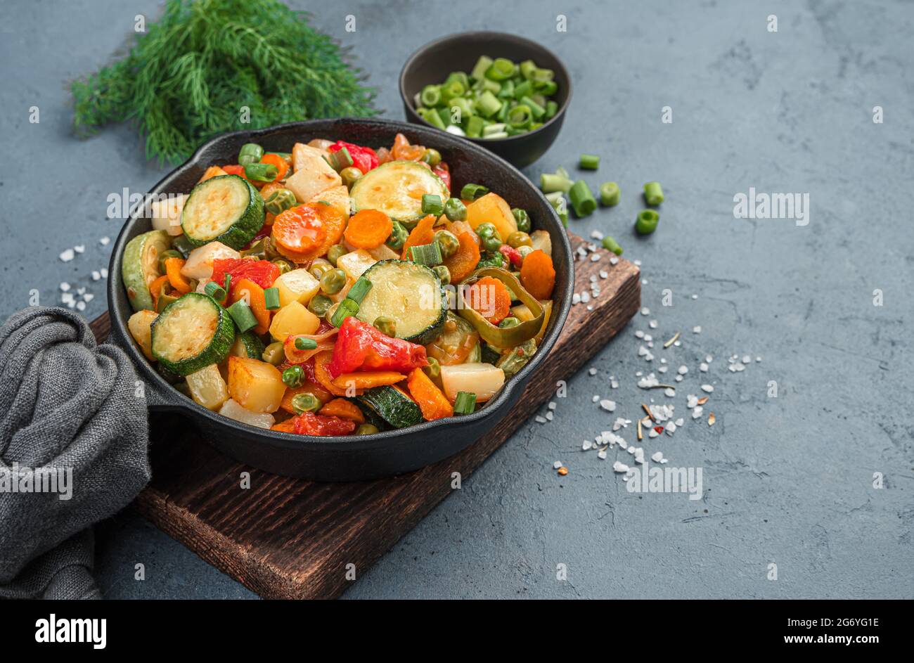 Fried vegetables in a frying pan on a gray background with fresh herbs ...
