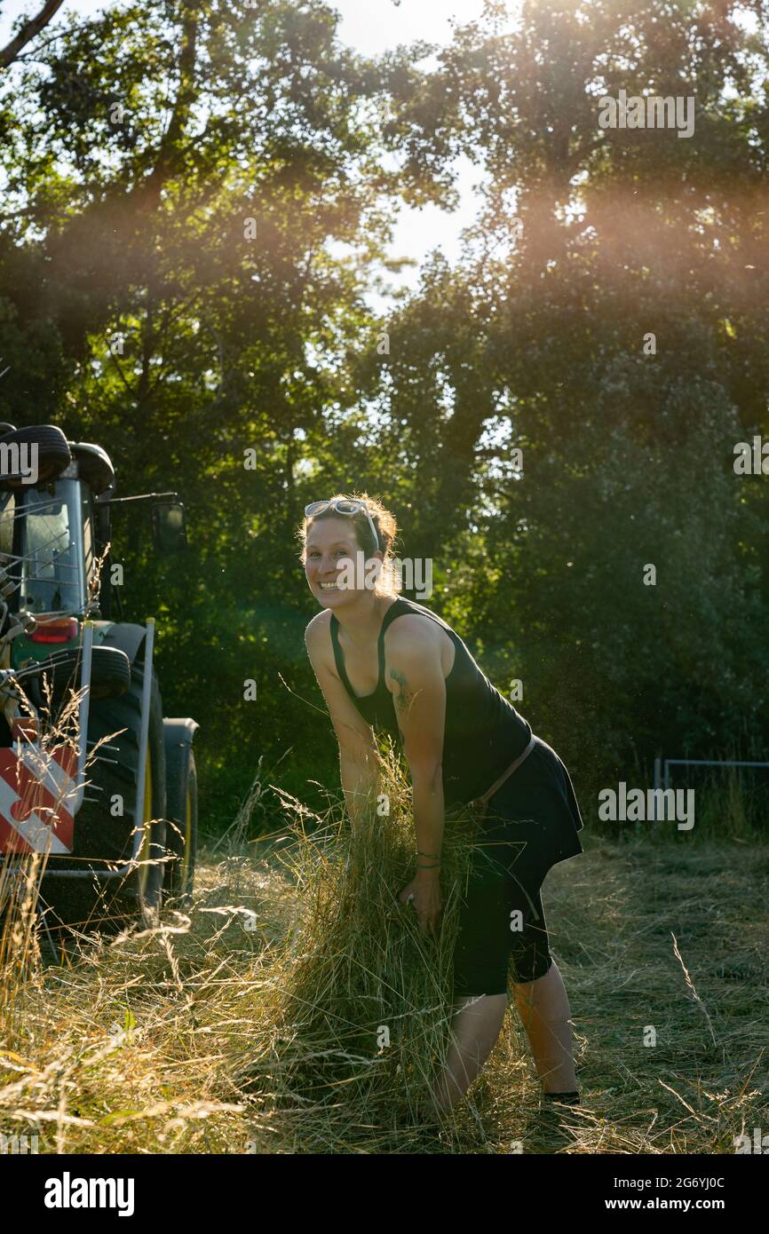 Charming young farmer woman playing with hay in field in evening sun ...