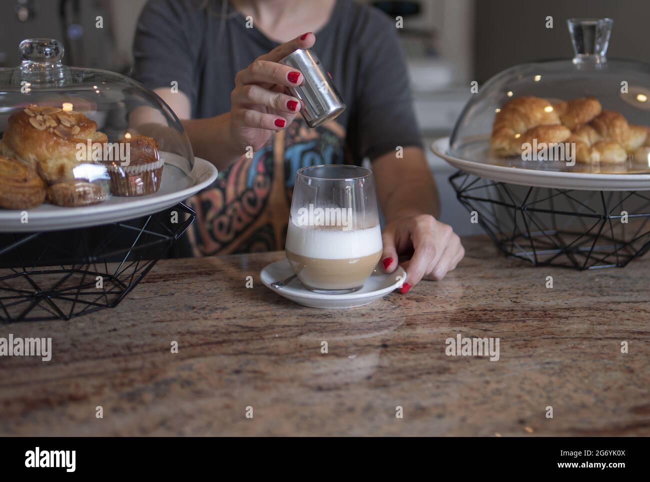 Female pouring chocolate powder on a glass of latte in between plates ...