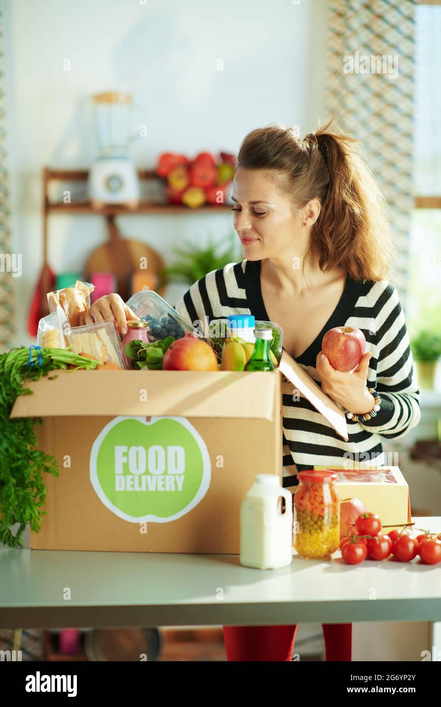 Food delivery. happy young woman with food box and apple in the kitchen ...