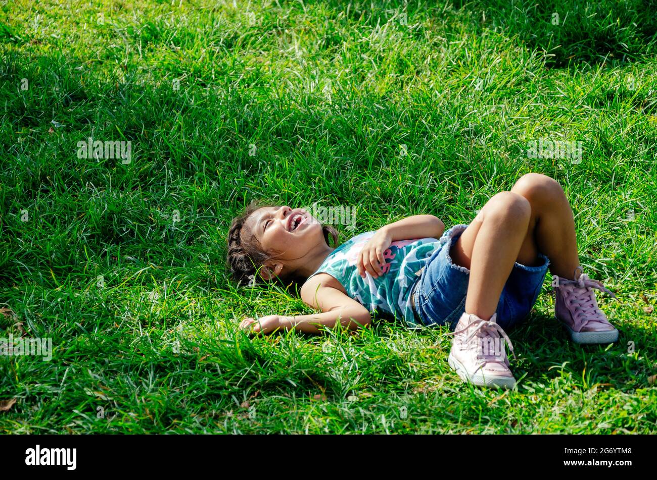 A little girl is smiling lying on the bright green grass. Portrait of a ...