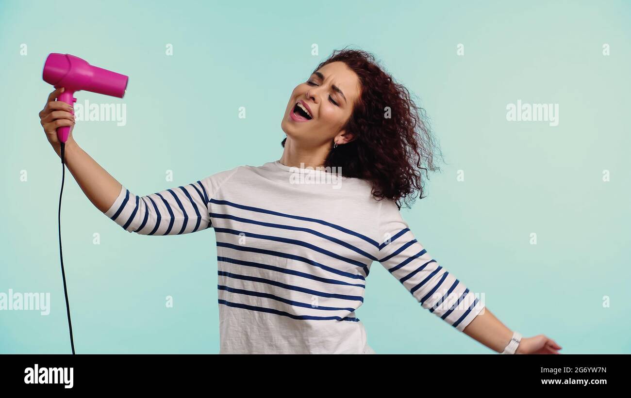 happy young woman drying curly hair and singing isolated on blue Stock ...