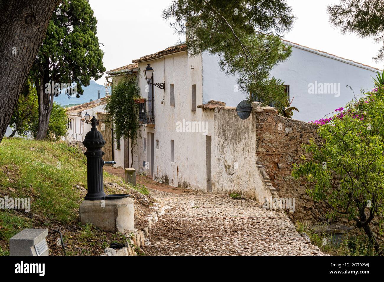 Country scenery with cobbled path, metal fountain, and white houses ...