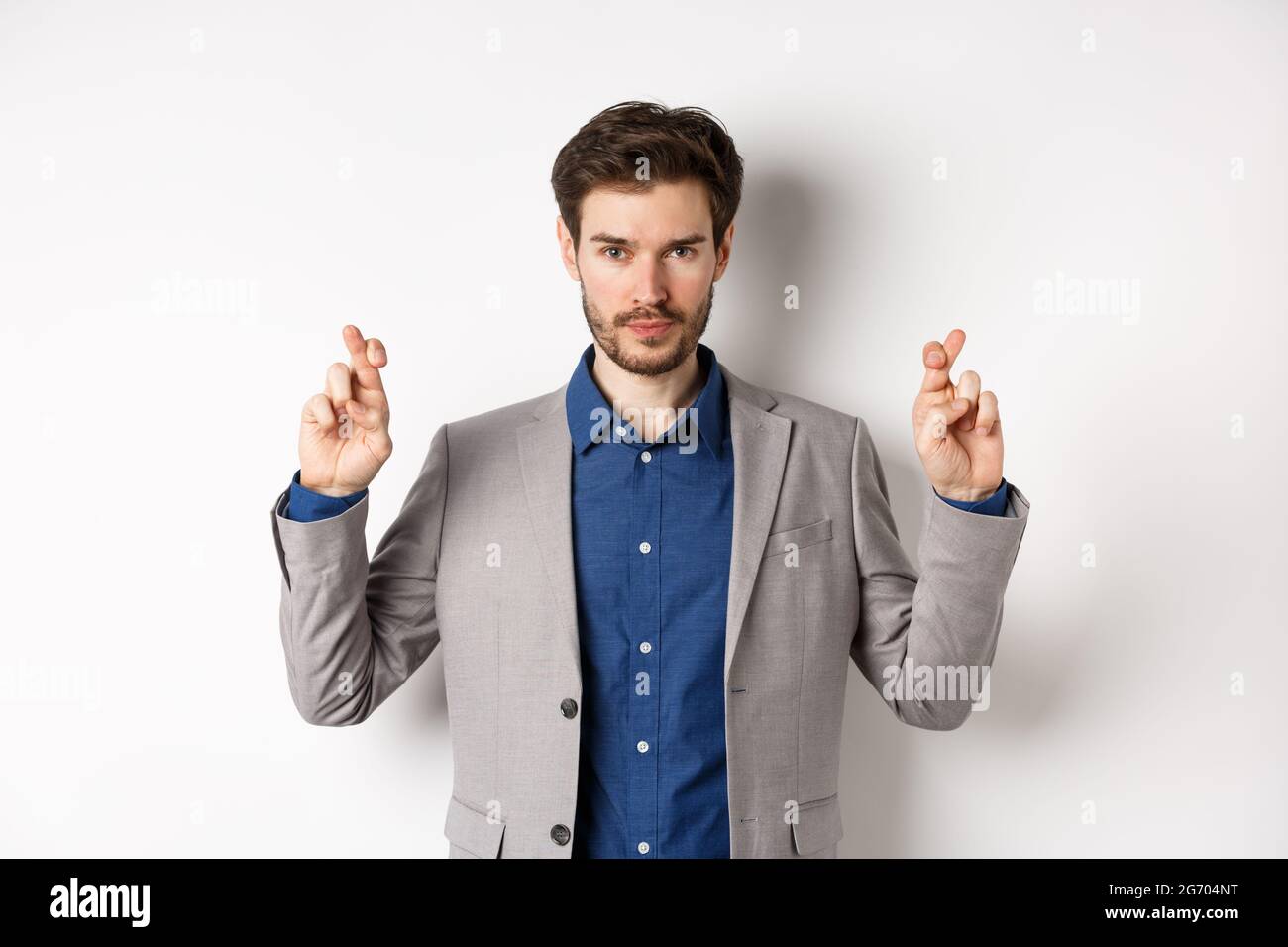 Hopeful man in suit cross fingers for good luck and looking confident ...
