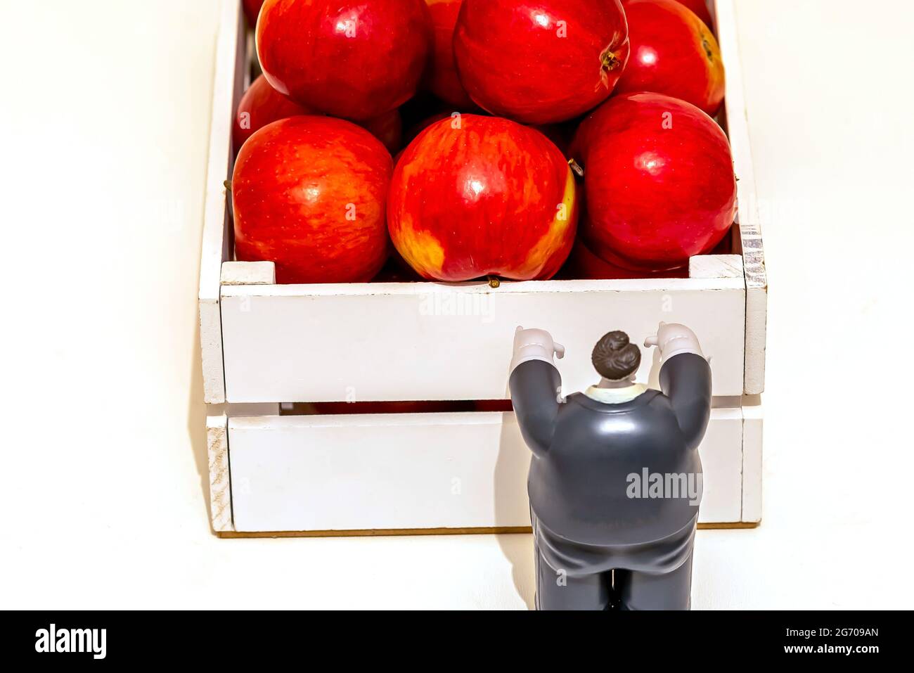 Small figure of a man holding a wooden box of red natural apples ...