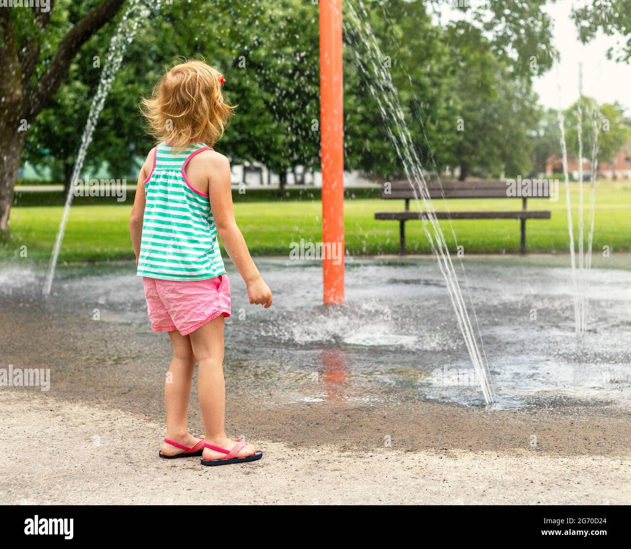 Little happy child playing with water at splash pad in the local public ...