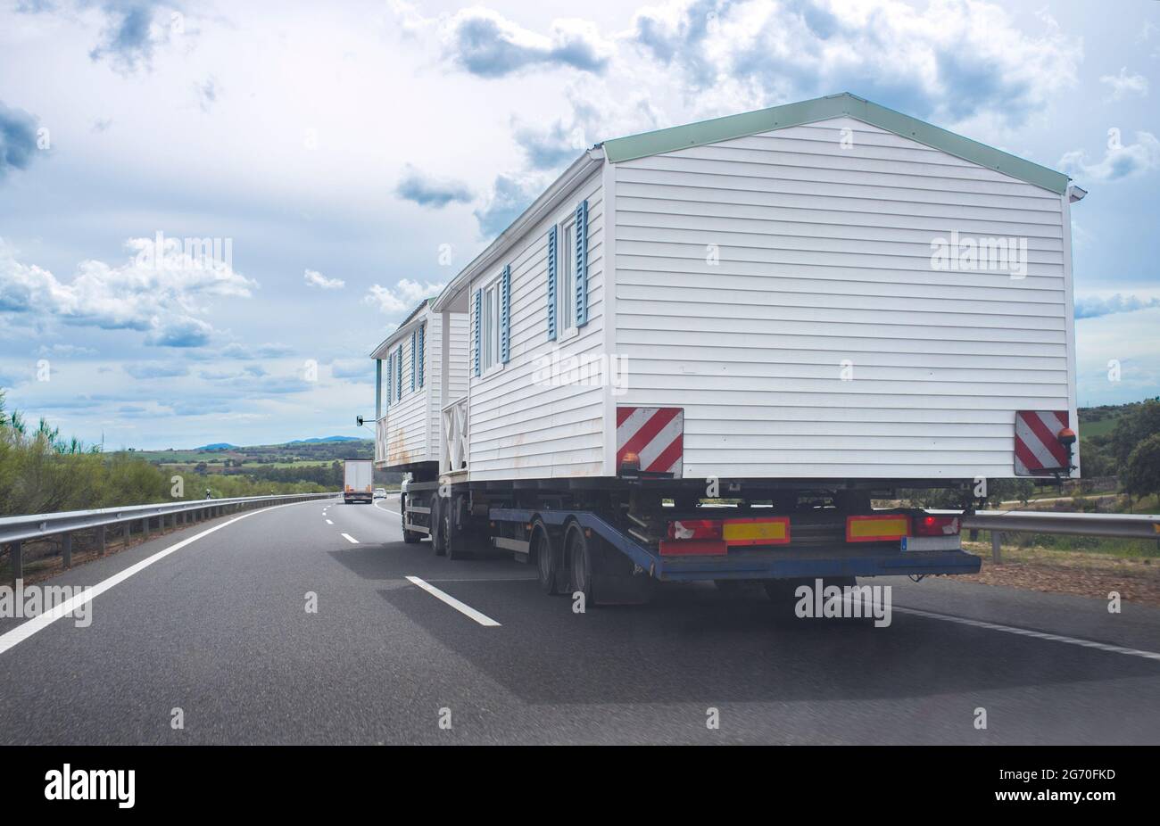 Driving behind heavy-duty truck carrying two prefabricated houses. View ...
