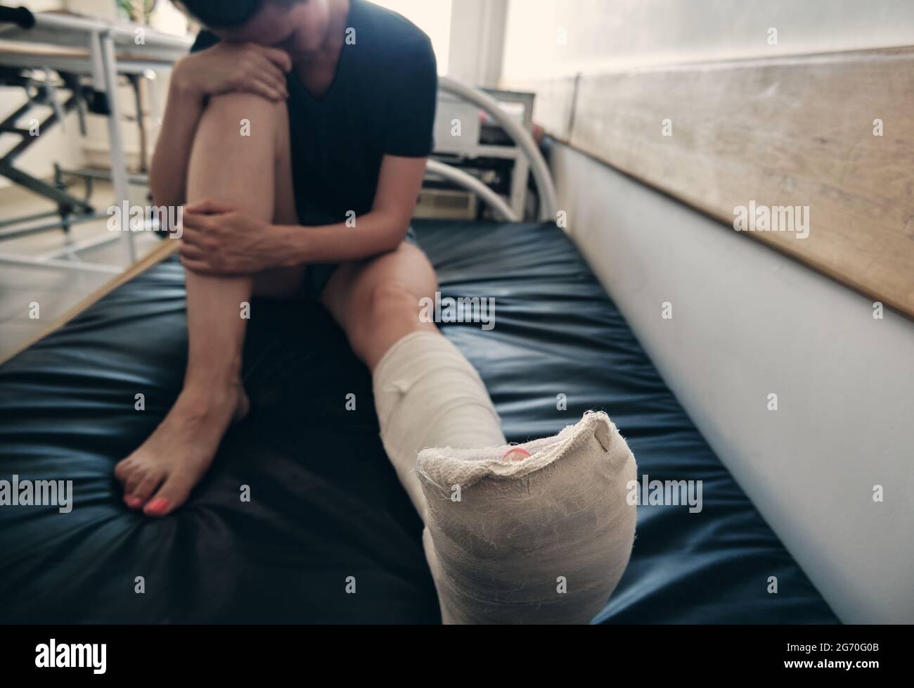 A woman with a broken leg sits on a hospital couch and regrets. Leg ...
