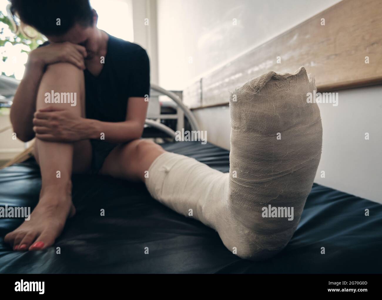 A woman with a broken leg sits on a hospital couch and regrets. Leg ...
