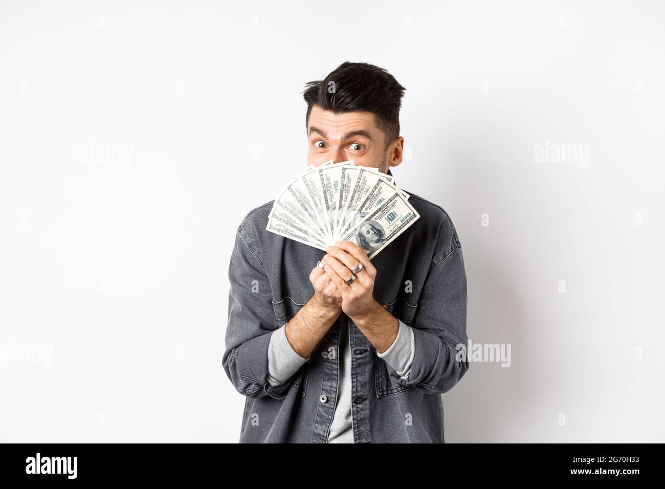 Excited funny guy hiding face behind dollar bills and smiling, showing ...