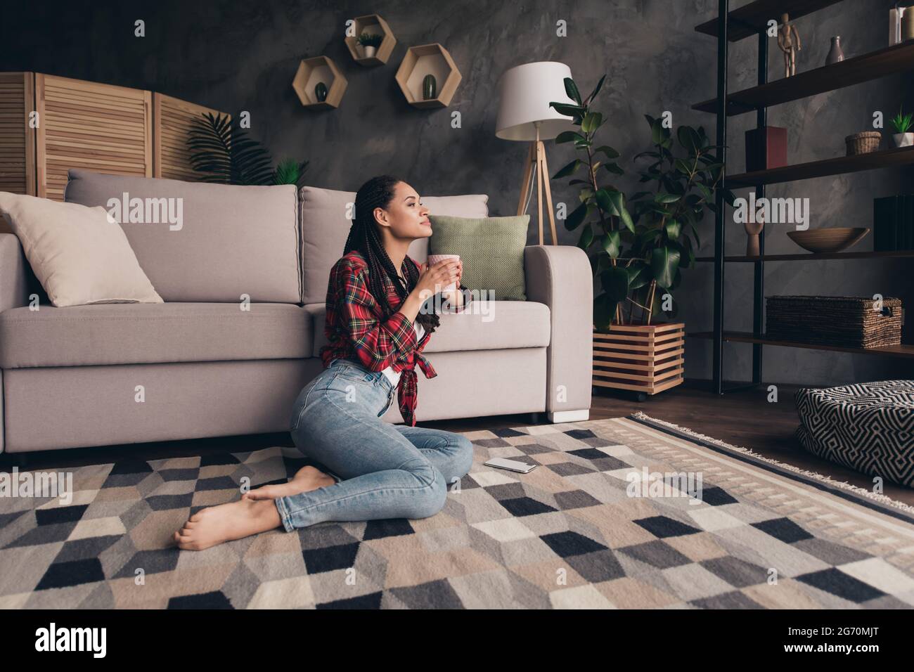 Portrait of attractive dreamy girl sitting on carpet drinking latte ...