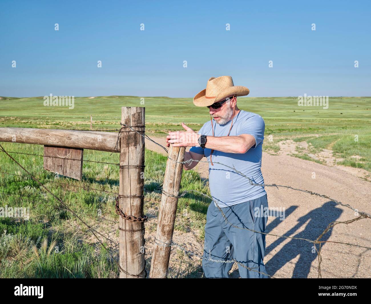 Senior man in a cowboy hat is opening or closing cattle barbed wire ...