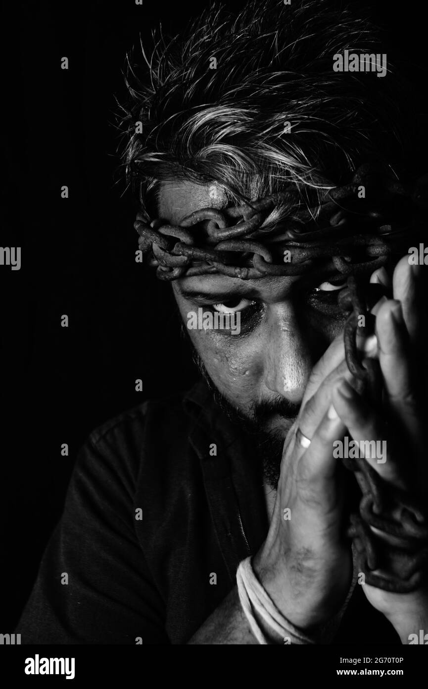 Grayscale portrait of an angry looking man with chained head and hands ...