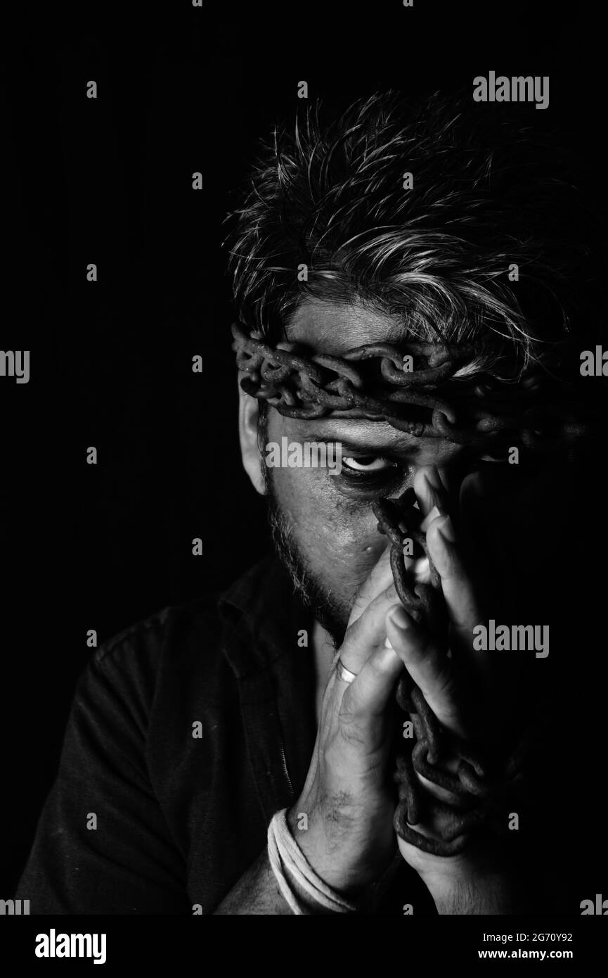 Grayscale portrait of a tortured man with chained head and hands on ...