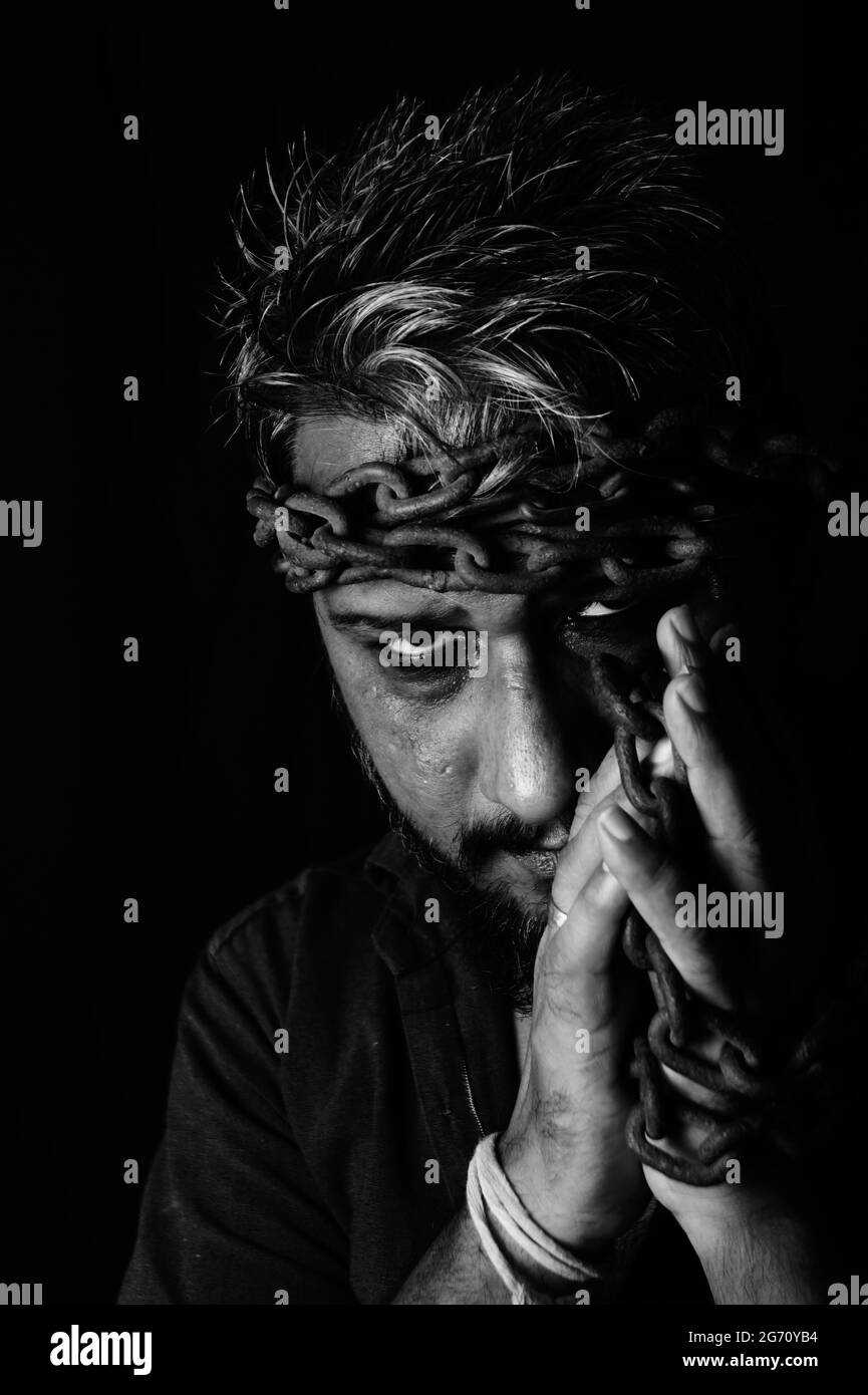 Grayscale portrait of a tortured man with chained head and hands and ...
