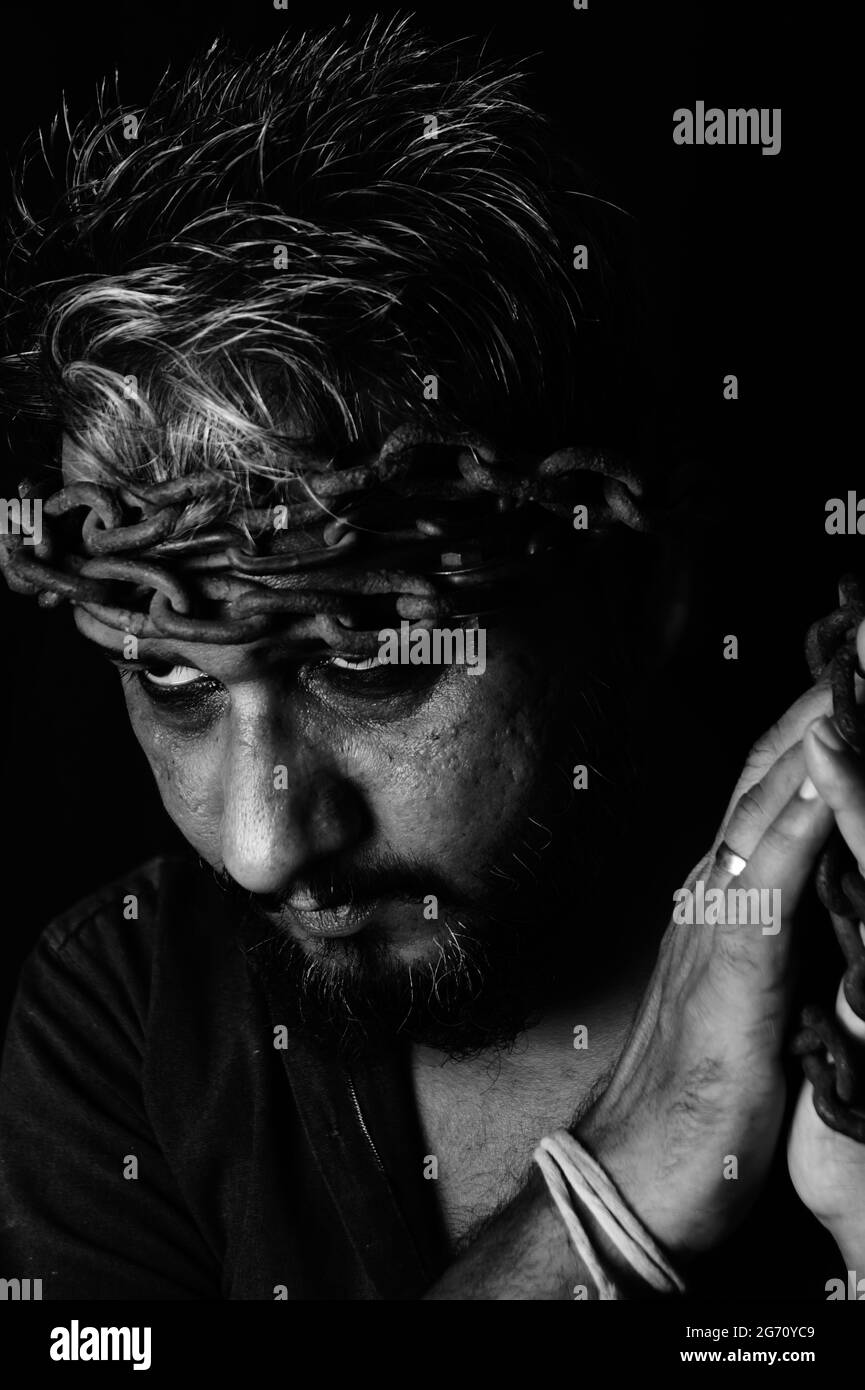 Grayscale portrait of a tortured man with chained head and hands ...