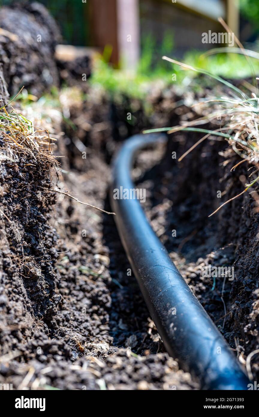 Focus on a black 1 inch sprinkler plastic water line laid in a shallow ...