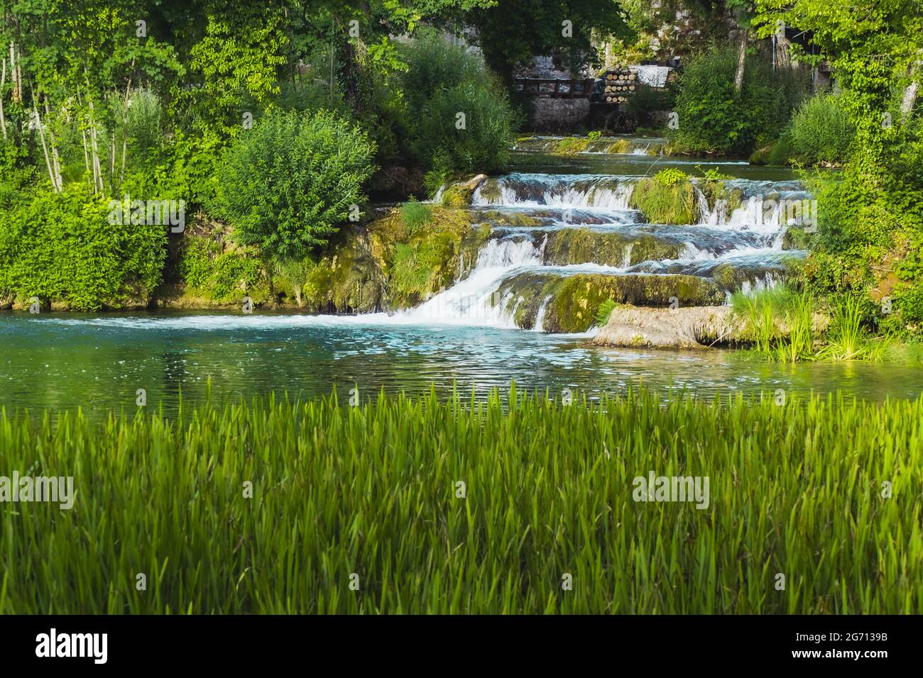 Front view of a small waterfall pouring down to river surrounded by ...