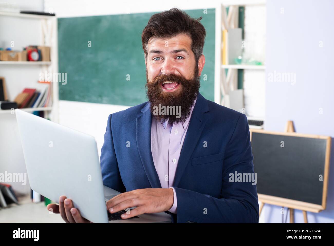 Smiling teacher with laptop notebook in classroom at school. Portrait ...