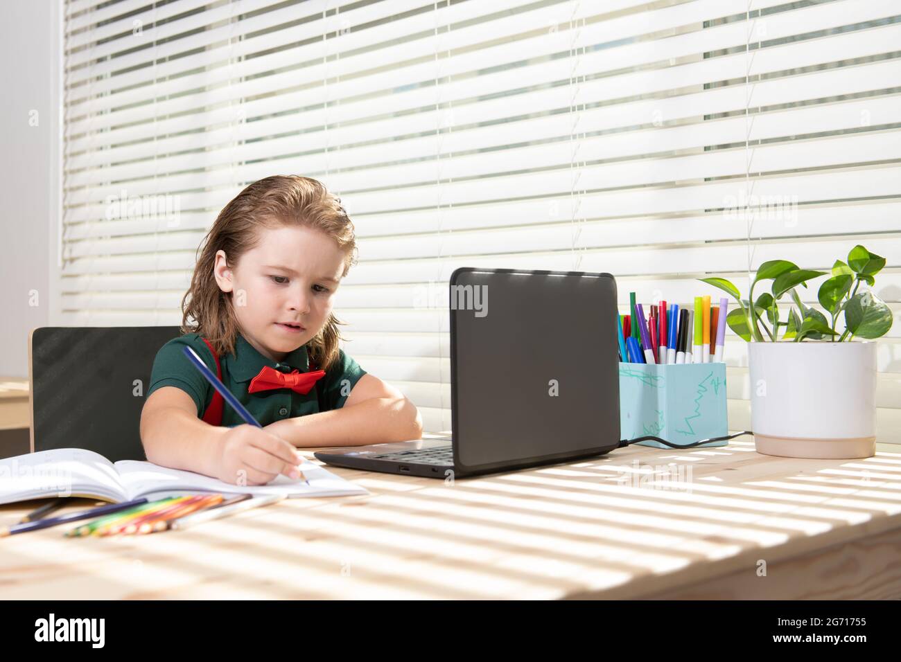 Little student schoolboy does her homework with a tablet or laptop at ...