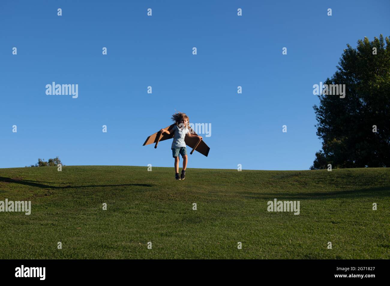Child running jumping and flying with toy plane wings on grass in park ...