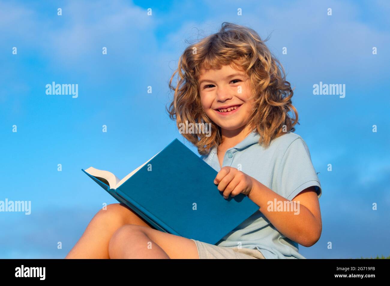 Cute lovely child reading book on blue sky background outside. Kid read ...