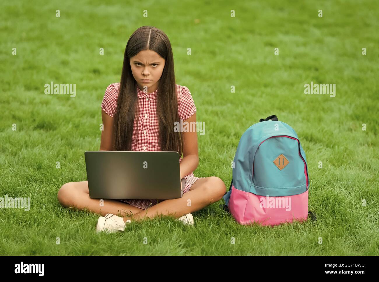 upset kid while using computer sit on green grass in park with school ...