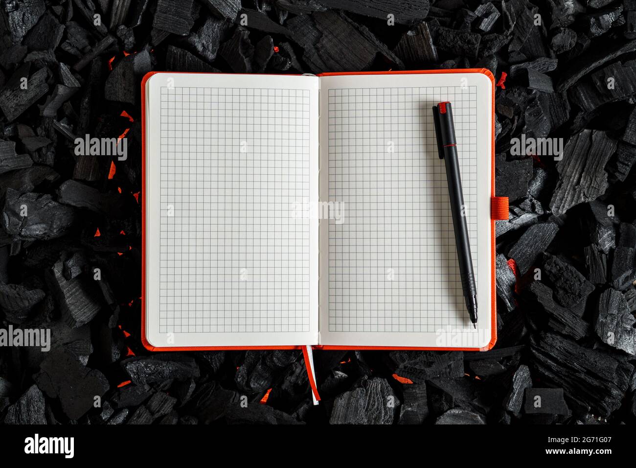 An open checkered notebook lying on a dark charcoal with red flashes of ...
