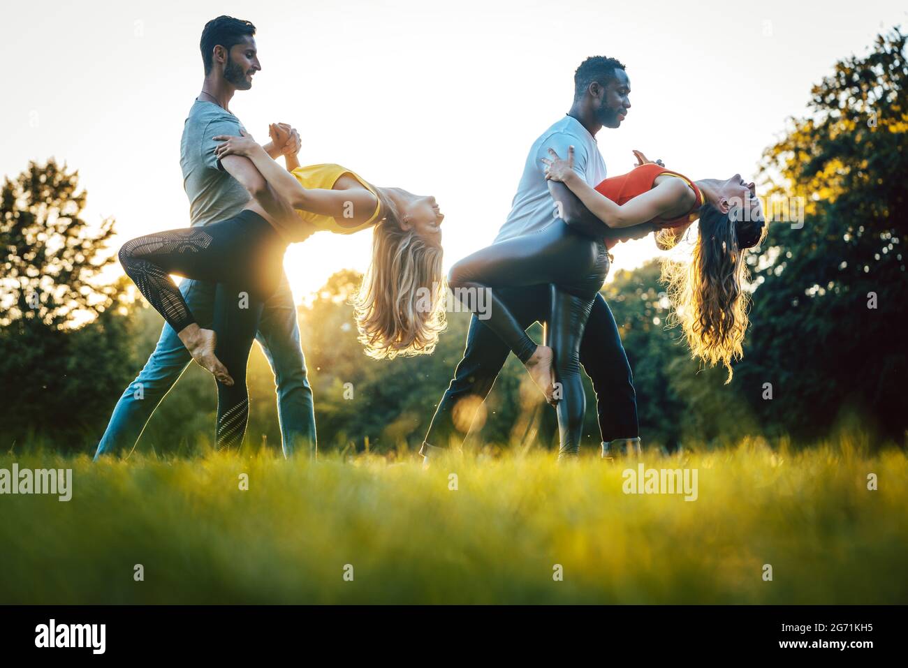 Women and men performing dance moves against backlit park Stock Photo ...