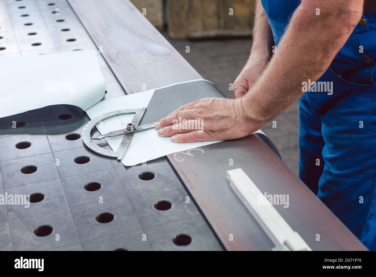Metalworker with angle meter measuring strip of metal for later cutting ...