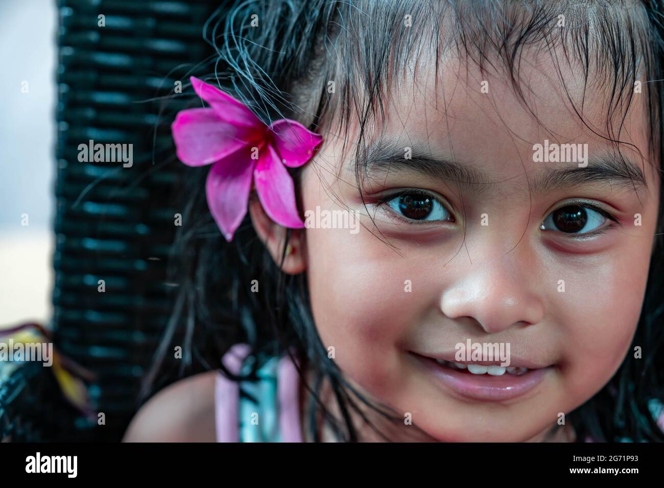 Little girl with large pink flower behind ear. Pretty asian child ...