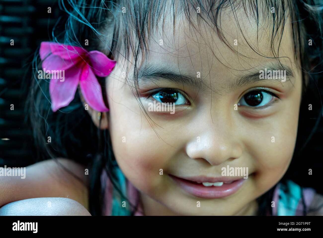 Little girl with large pink flower behind ear. Pretty asian child ...