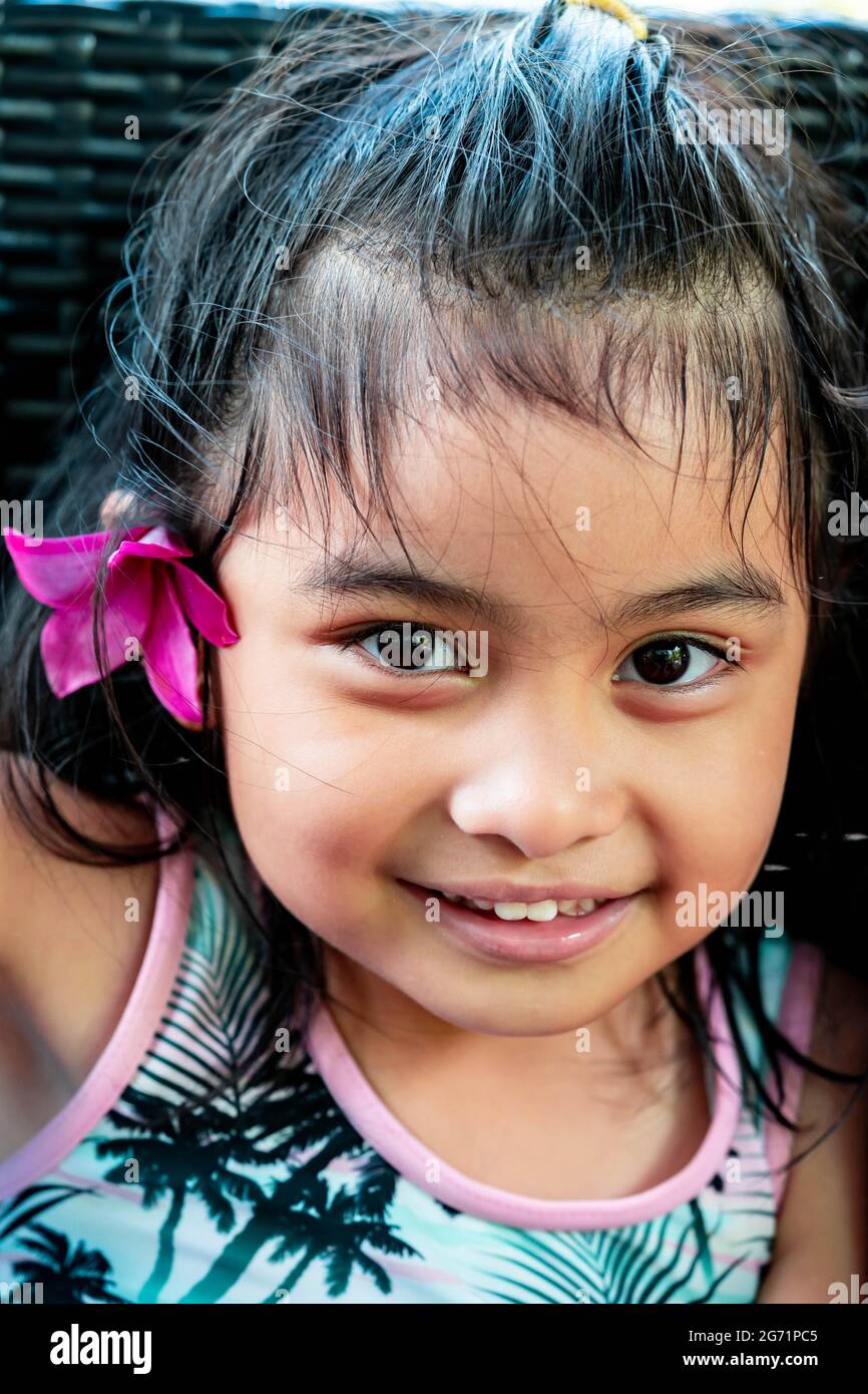 Little girl with large pink flower behind ear. Pretty asian child ...