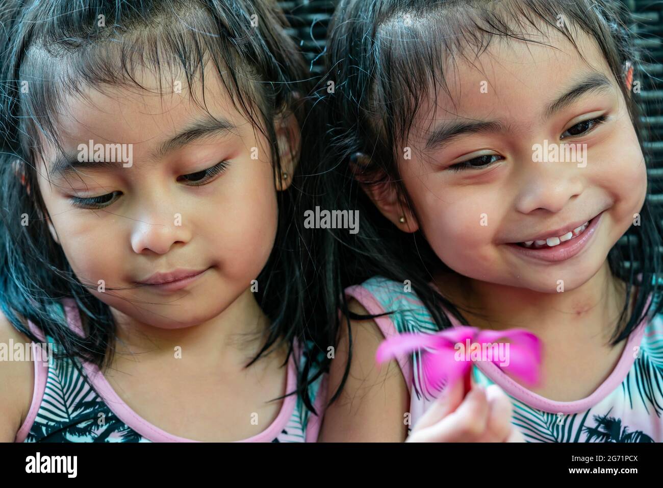 Pretty child twins holding a pink flower. Pretty asian twins portrait ...