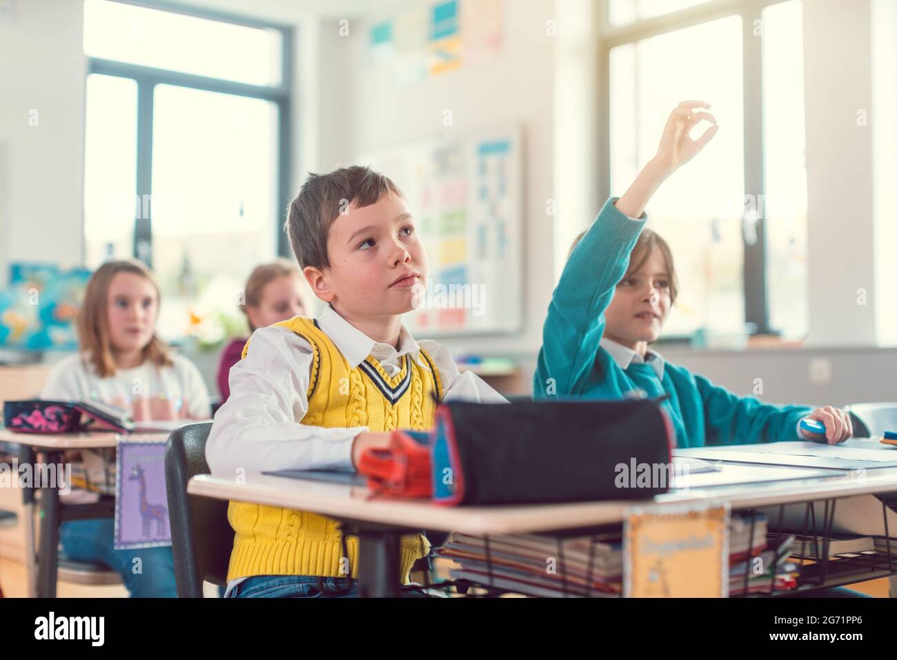 Boy student in class of elementary school knowing an answer raising his ...