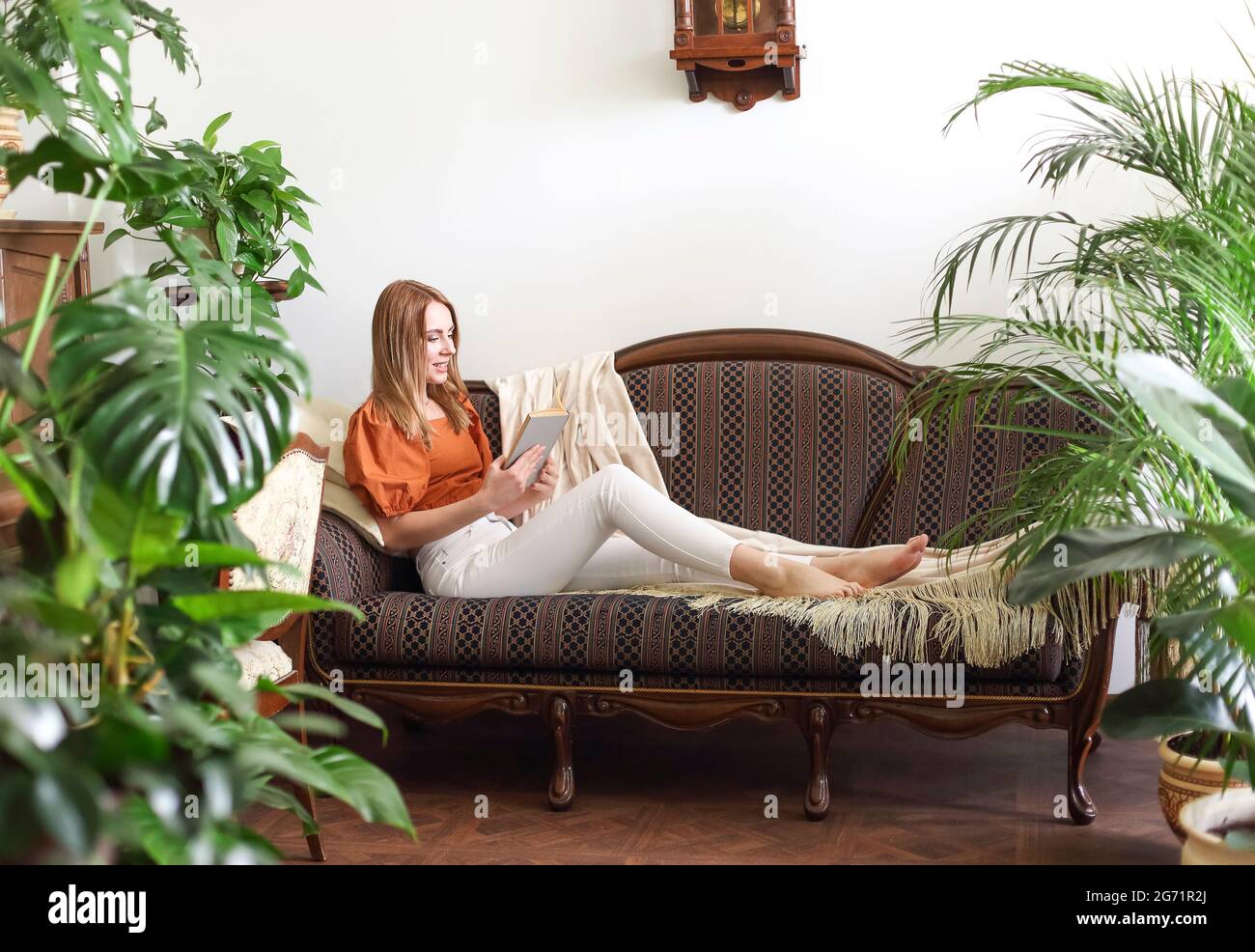 Full body barefoot female relaxing on couch and reading interesting ...