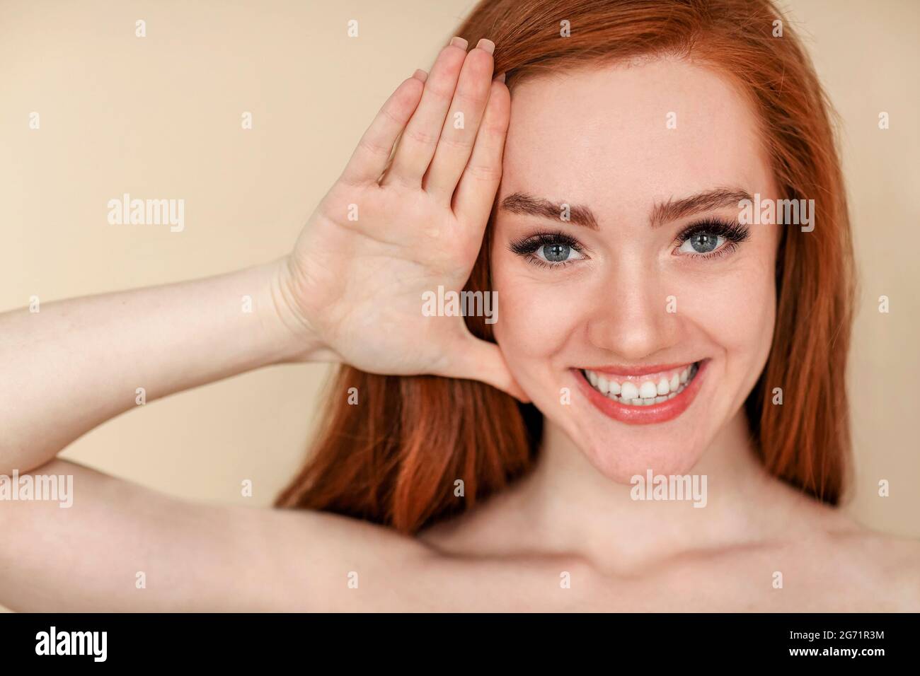 Young ginger female with clean skin touching face and looking at camera ...