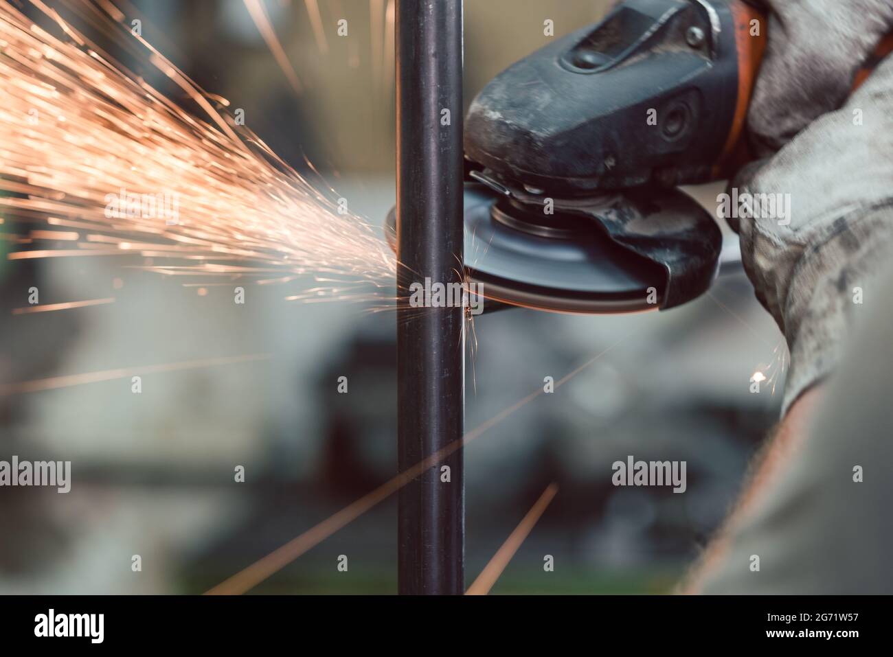 Worker in metal factory grinding workpiece with disk grinder, sparks ...