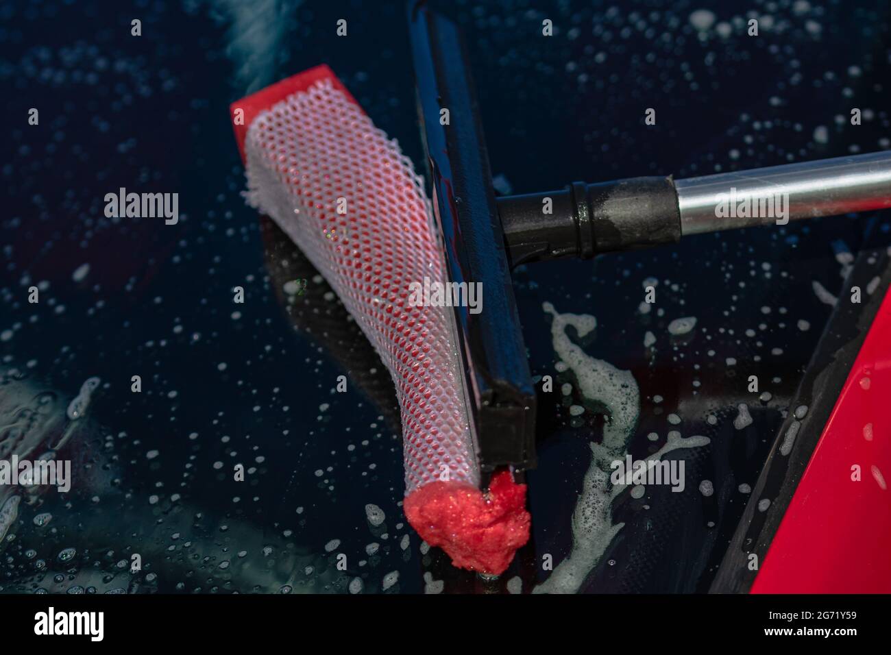 Washing and cleaning the front window of a car with mop in self service ...