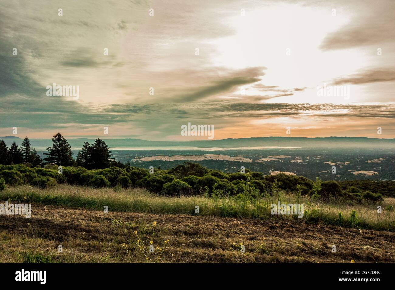 Landscape of a field covered in greenery with a town under a cloudy sky ...