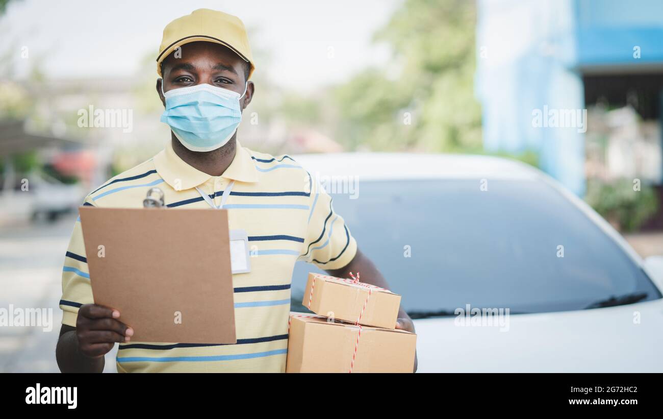 African delivery man with face mask holding a box package and cardboard ...